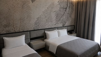 Quarto de hotel com duas camas, uma grande obra de arte abstrata na parede, uma mesa de cabeceira e uma janela com cortinas.