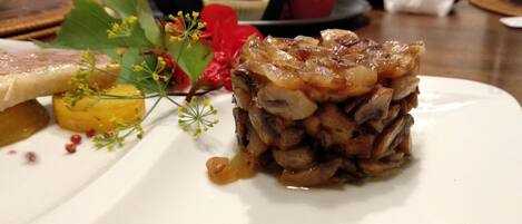 Um prato com uma pilha de cogumelos coberta com cebolas caramelizadas, acompanhada por uma fatia de batata amarela e alguns enfeites.