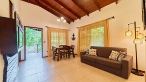 Uma sala de estar com sofá, mesa de jantar, cadeiras, televisão e ventilador de teto.