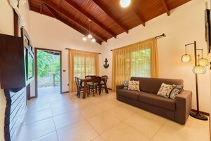Uma sala de estar com sofá, mesa de jantar, cadeiras, televisão e ventilador de teto.
