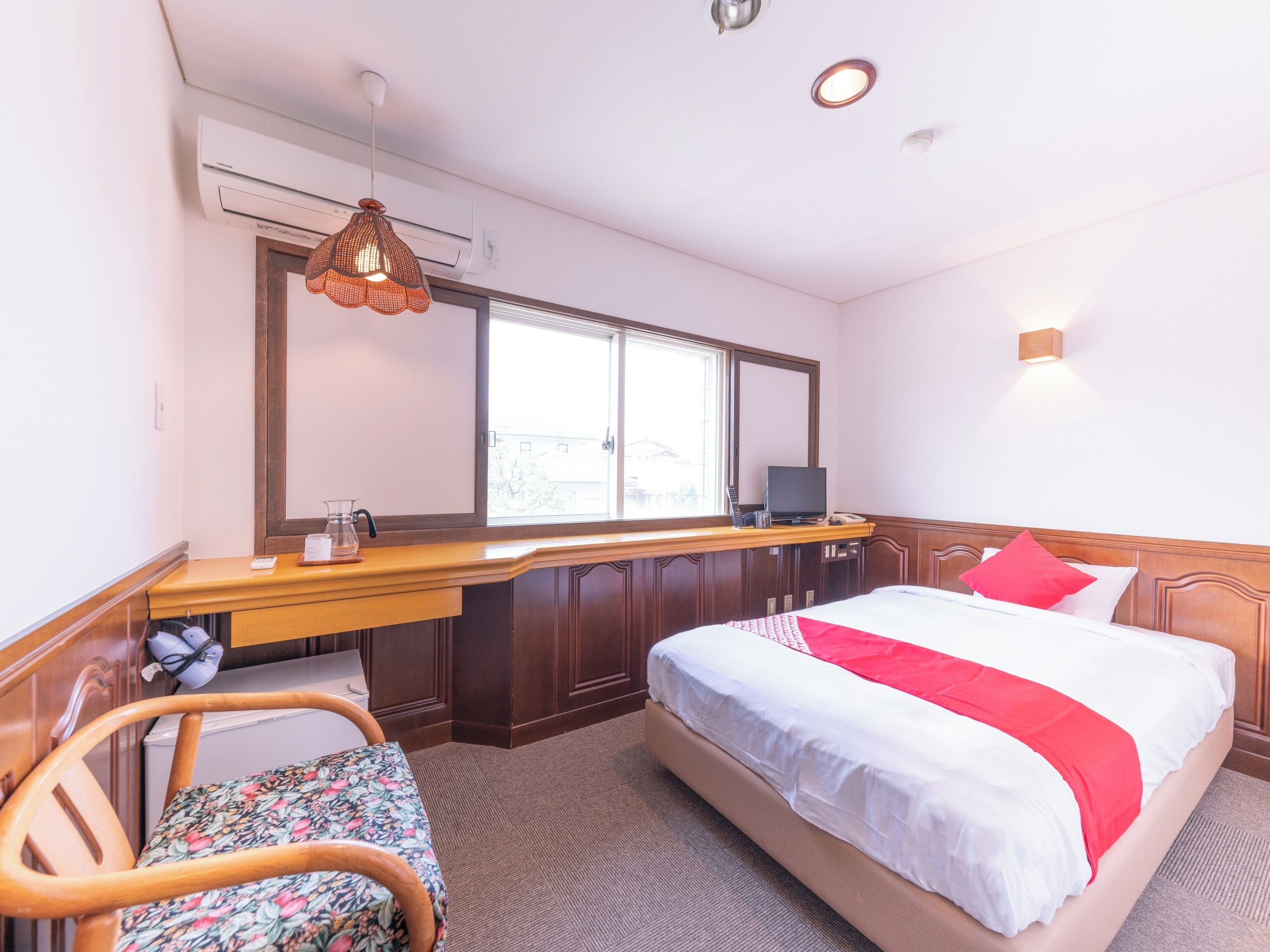 Quarto de hotel com uma cama, uma escrivaninha com computador, uma cadeira e uma janela.