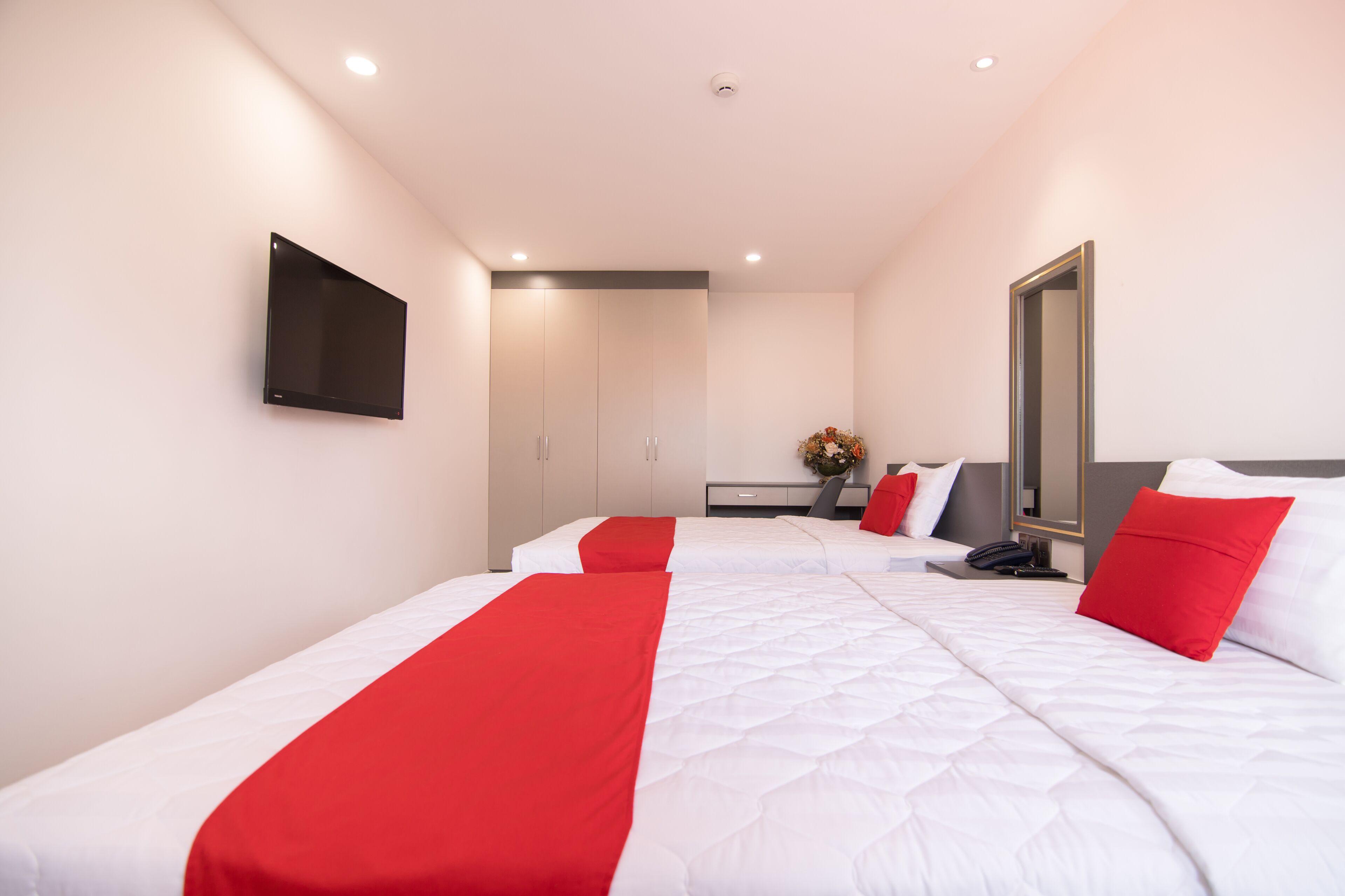 Quarto de hotel com duas camas, uma televisão fixada na parede, uma mesa com uma cadeira e um espelho.