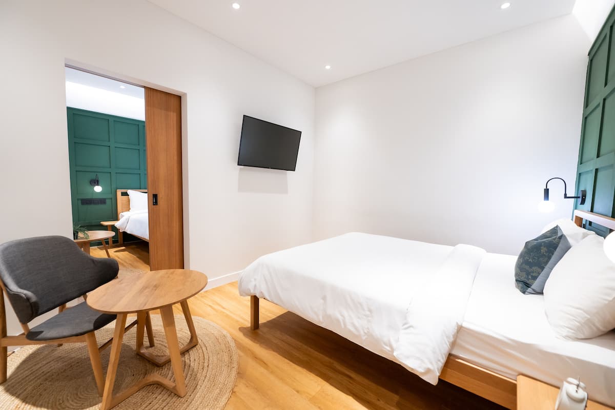 Quarto de hotel moderno com uma cama, uma TV, uma cadeira e uma mesinha.