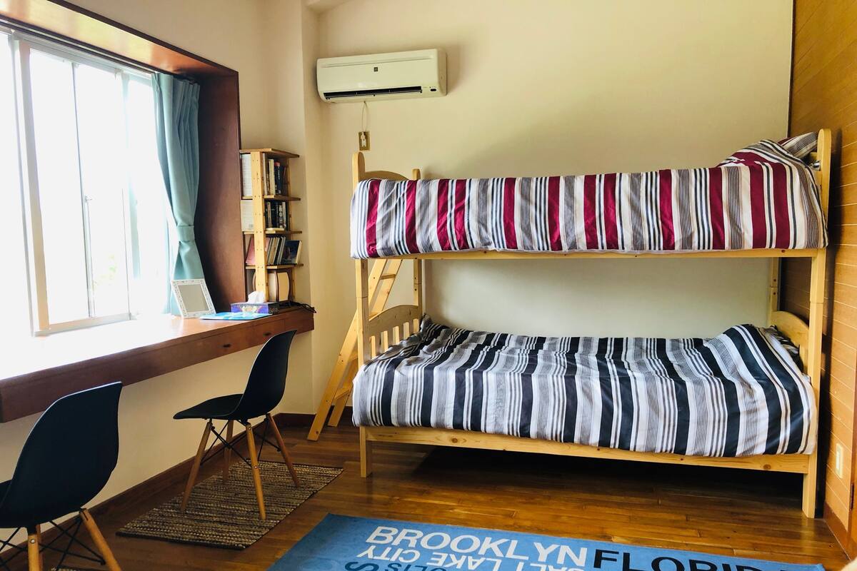 Quarto com beliche, escrivaninha, cadeira e tapete com nomes de cidades.