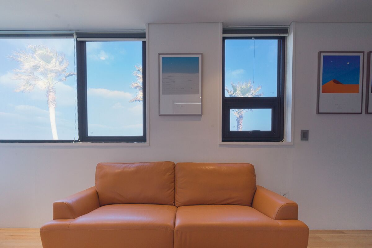 Quarto com sofá de couro, janelas amplas e quadros nas paredes.