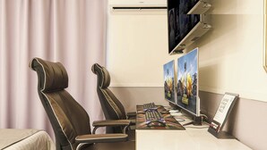 Quarto de hotel com duas poltronas reclináveis, uma mesa com computador e um quadro na parede.