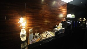 Quarto de hotel com parede de madeira, divisória de vidro, máquina de café e bandeja com itens de café da manhã.