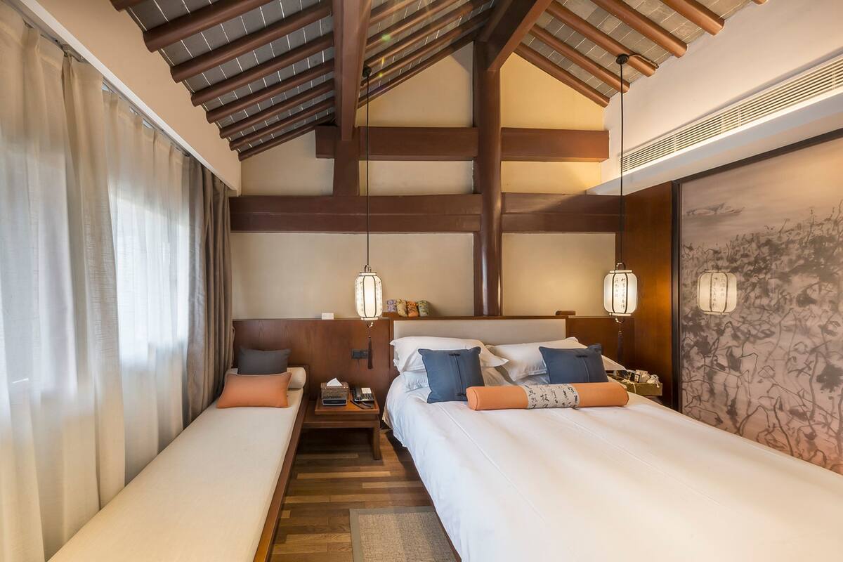 Quarto de hotel com duas camas, vigas de madeira, uma janela grande com cortinas e uma parede em estilo tradicional japonês.