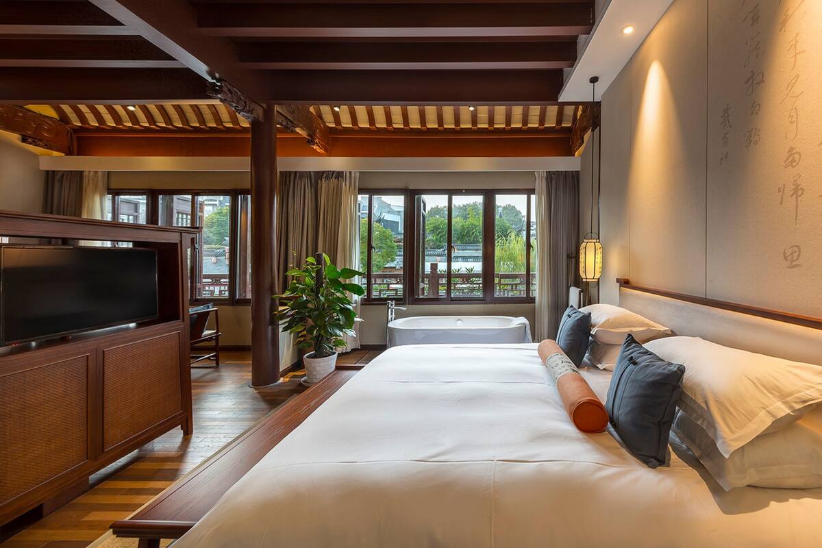 Quarto de hotel com uma cama grande, televisão, varanda e uma parede com caligrafia.