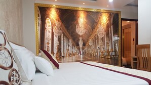 Quarto de hotel luxuoso com uma cama grande, um espelho refletindo um amplo corredor e um candelabro.