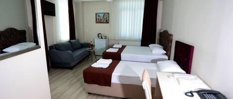 Quarto de hotel com duas camas, uma escrivaninha, uma cadeira, uma mesinha com chaleira e uma televisão fixada na parede.