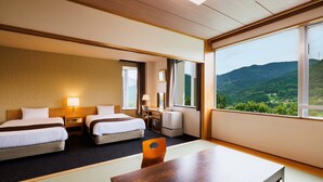 Quarto de hotel com duas camas, uma escrivaninha e uma janela grande com vista para colinas verdes.
