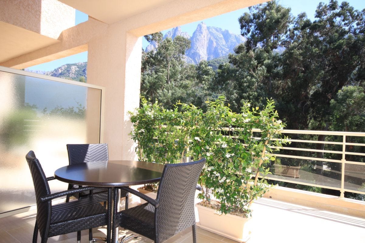 Varanda com uma mesa redonda e quatro cadeiras, com vista para uma paisagem montanhosa com árvores densas.