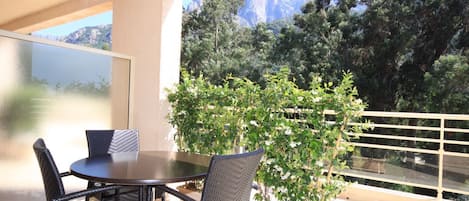 Varanda com uma mesa redonda e quatro cadeiras, com vista para uma paisagem montanhosa com árvores densas.