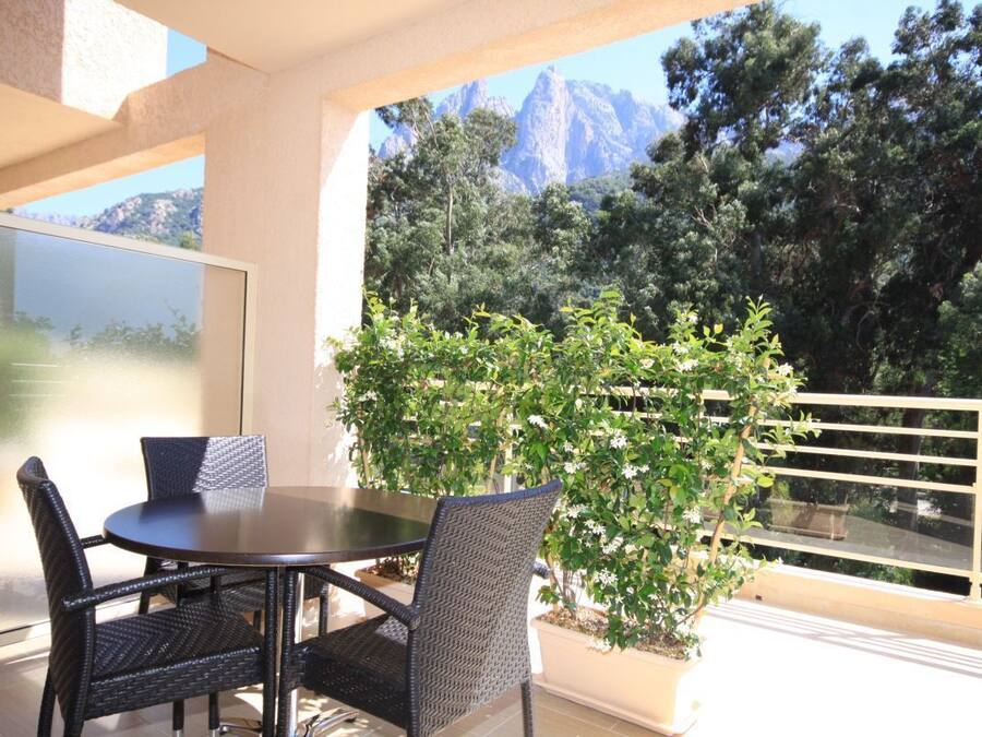 Varanda com uma mesa redonda e quatro cadeiras, com vista para uma paisagem montanhosa com árvores densas.