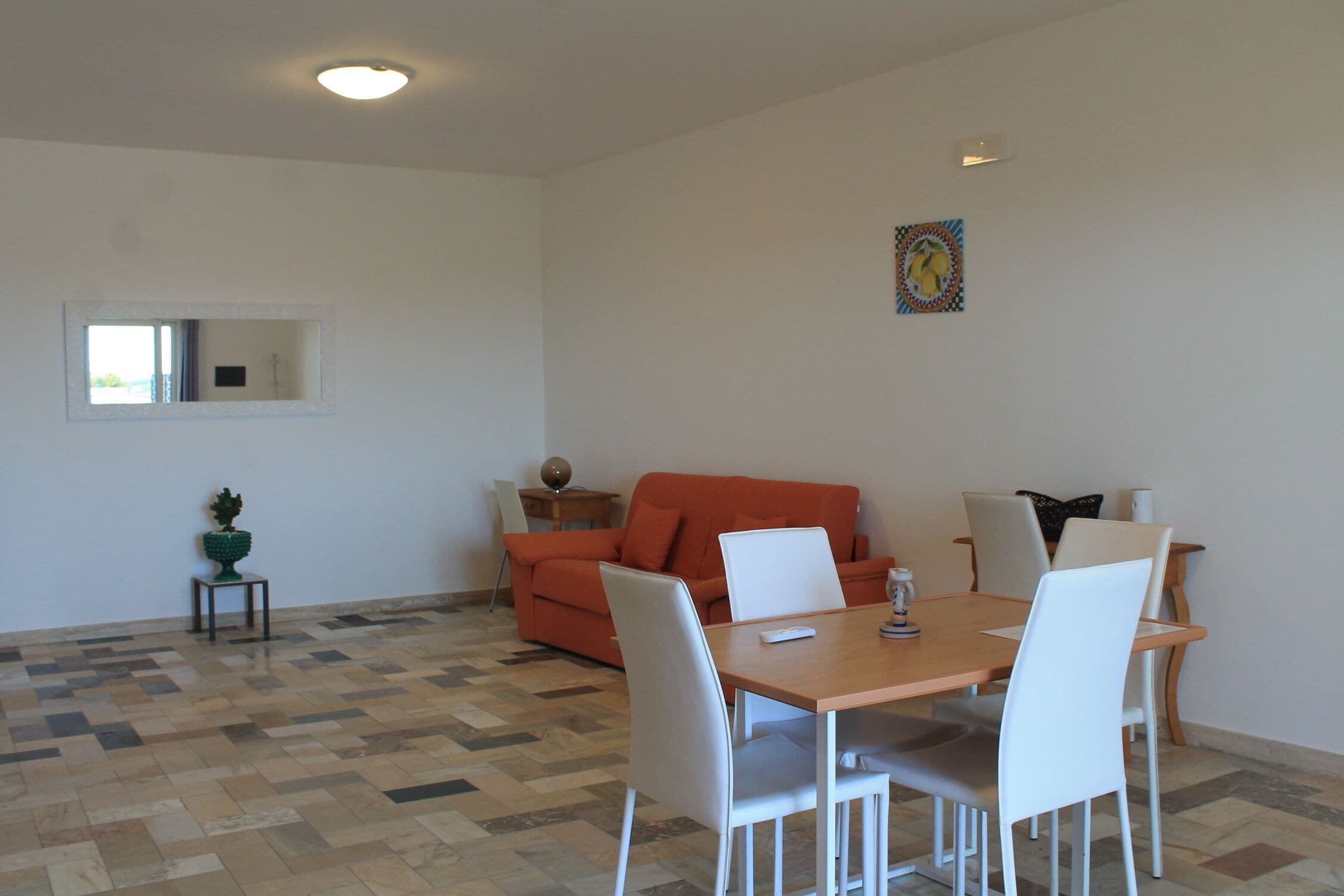 Uma sala de jantar com mesa de madeira e cadeiras brancas, um sofá laranja e uma pequena mesa lateral com um globo e uma planta.