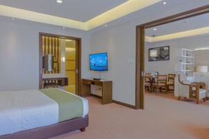 Quarto de hotel com cama, escrivaninha, televisão e área de refeições.