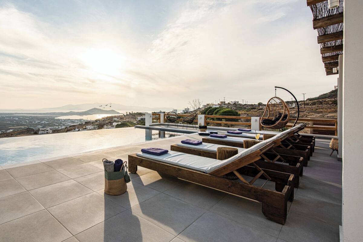 Piscina infinita com espreguiçadeiras e cadeira de vime com vista para uma paisagem deslumbrante.