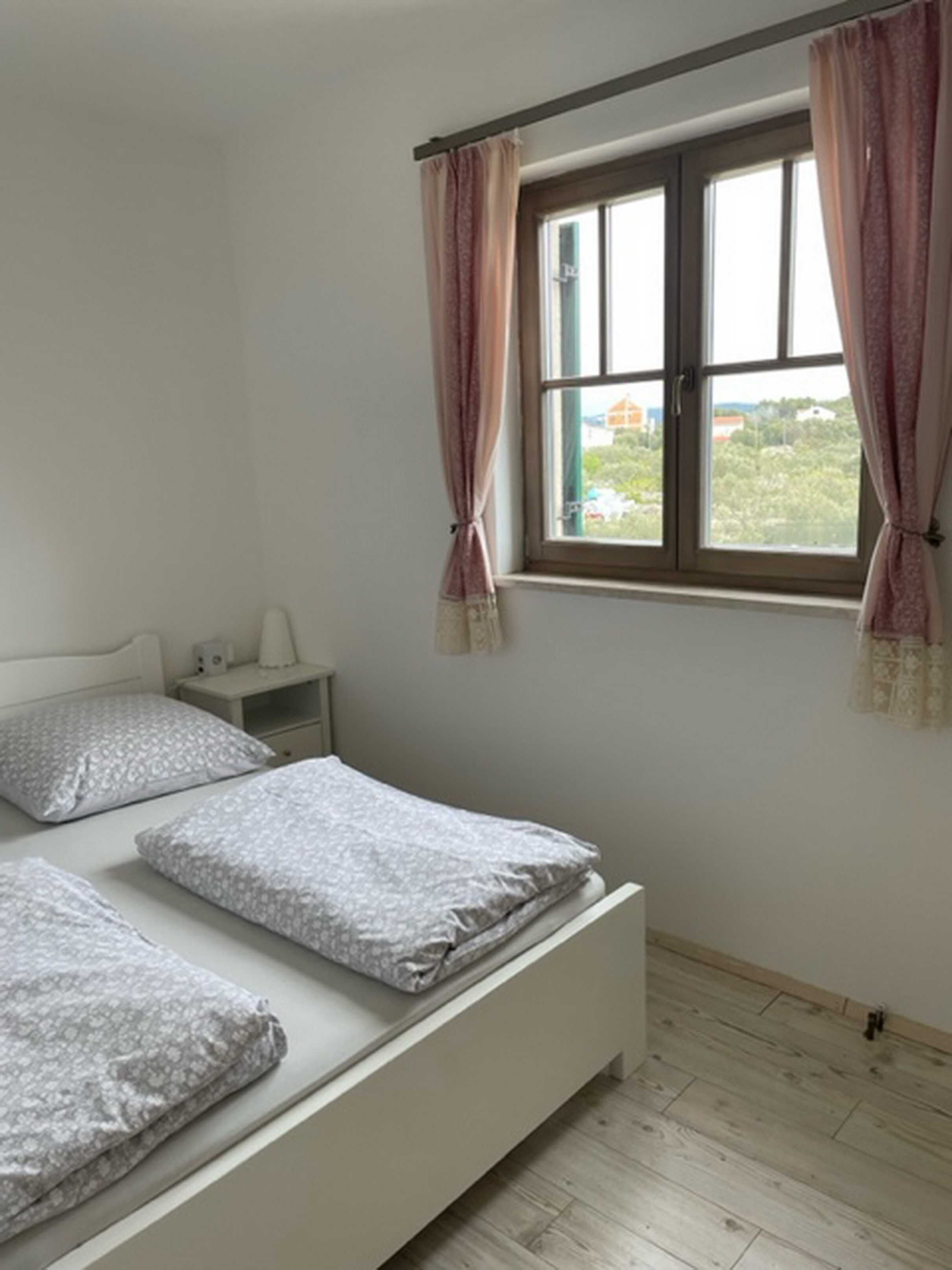Quarto com uma cama de solteiro, uma mesinha de cabeceira e uma janela com cortinas.