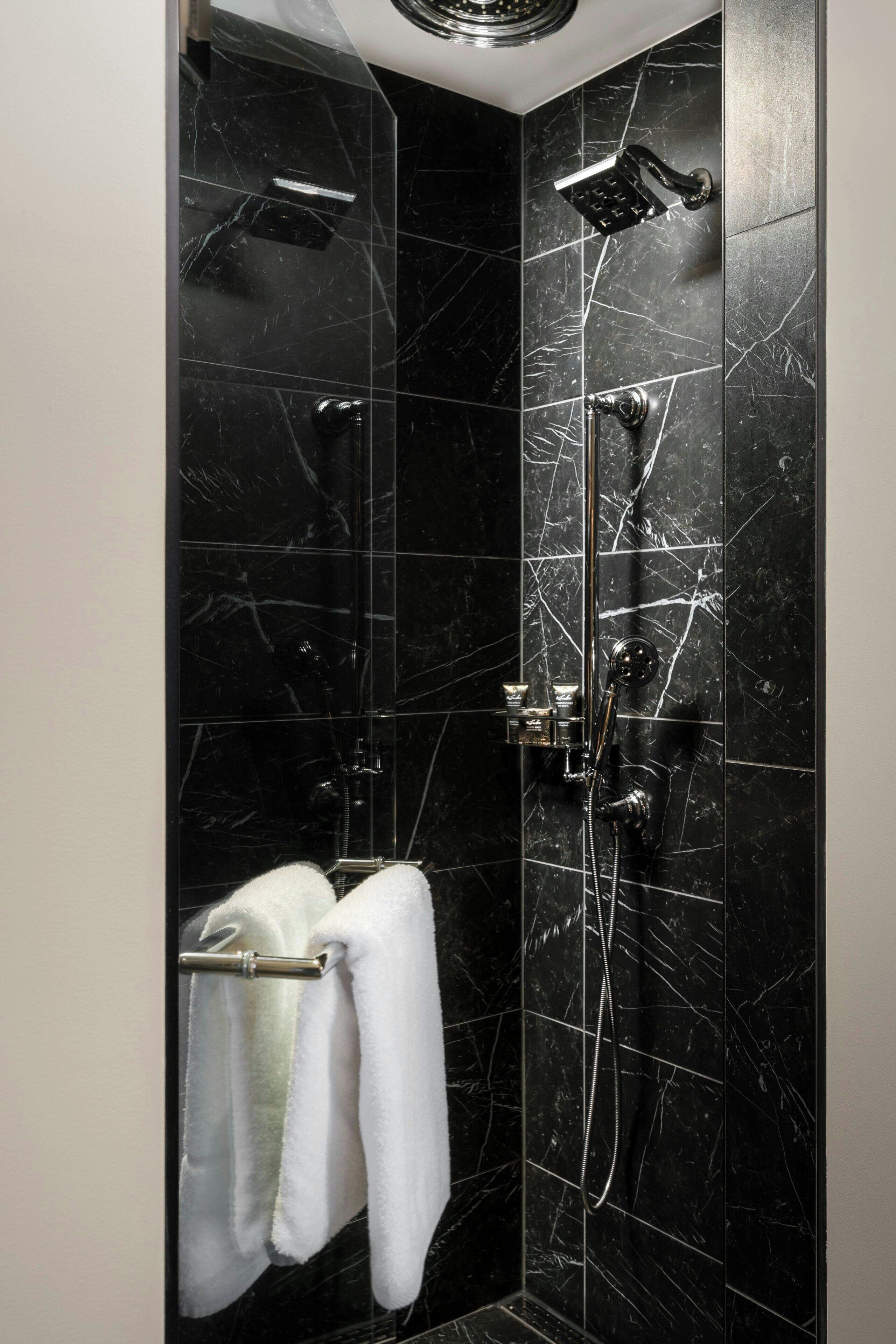 Um chuveiro moderno com azulejos de mármore preto, um chuveiro manual e um porta-toalhas com duas toalhas brancas.