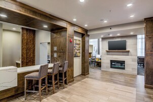 Um interior moderno com área de bar, assentos, lareira e uma grande tela de TV.