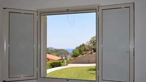 Quarto com uma janela grande que oferece vista para uma paisagem verde e um corpo d'água distante.
