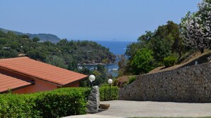 Um imóvel costeiro com um muro de pedra, entrada pavimentada e vista para o mar e colinas.