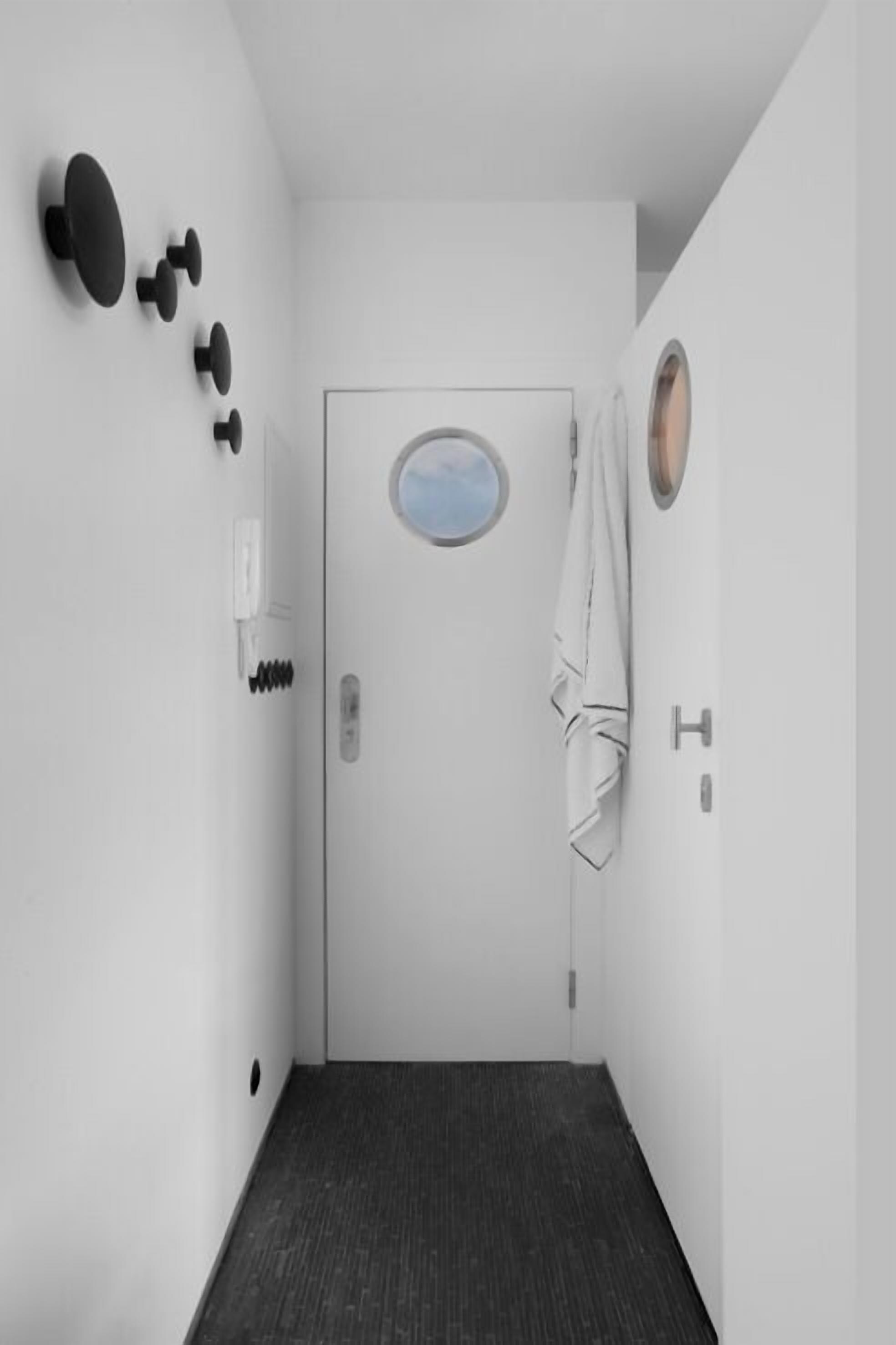 Um corredor estreito com uma porta branca, uma toalha pendurada na parede e uma pequena janela.