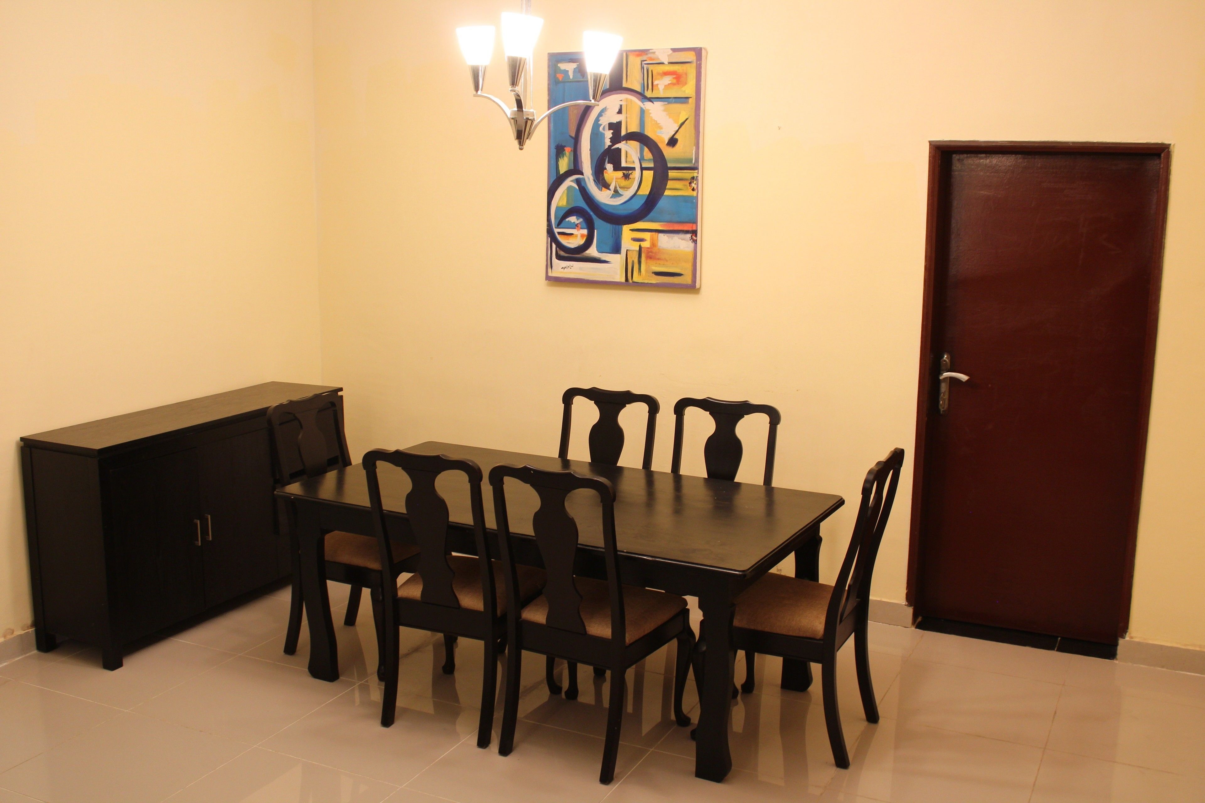 Uma sala de jantar com uma mesa retangular, seis cadeiras, um armário preto e uma porta.