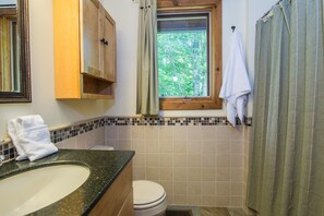 Casa de banho com lavatório, sanita e janela com vista para o verde.