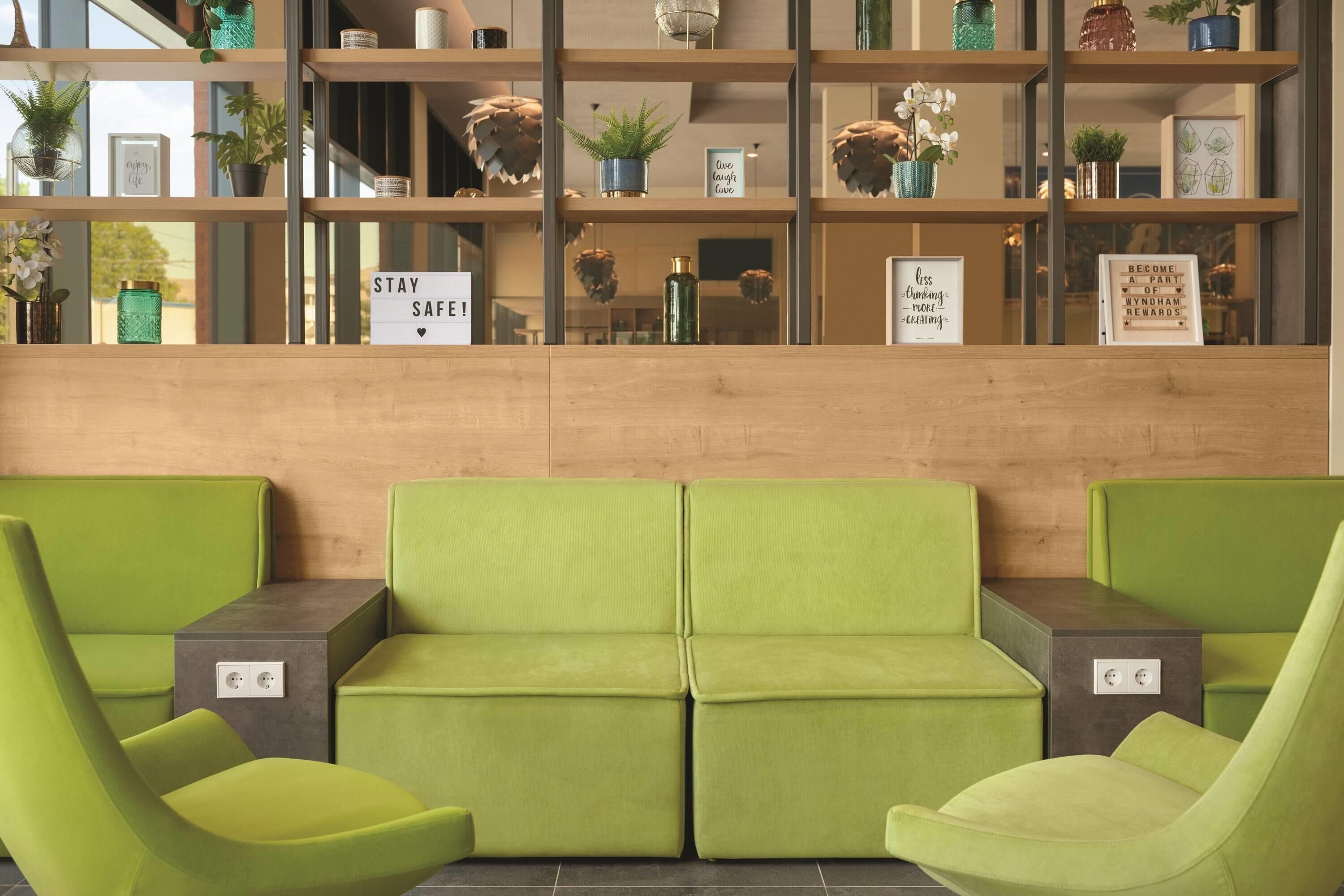 Uma área de recepção com um sofá verde, um balcão de madeira e uma estante com diversos objetos decorativos e placas.