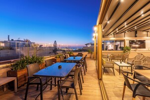 Um pátio externo com mesas e cadeiras, vista para a paisagem urbana e um edifício com design moderno.