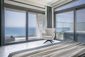 Quarto moderno com uma cama grande, uma cadeira e varanda com vista para o mar.