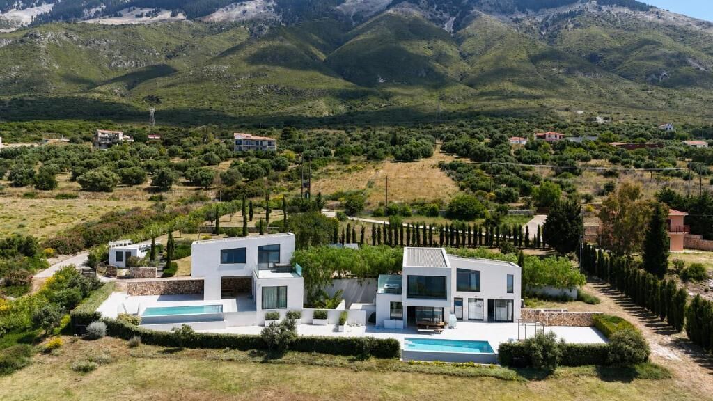Uma casa moderna de dois andares com piscina, rodeada por um jardim bem cuidado e um cenário montanhoso.