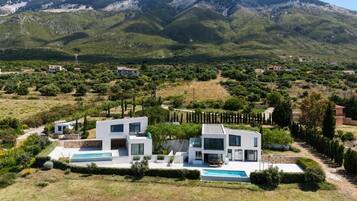Uma casa moderna de dois andares com piscina, rodeada por um jardim bem cuidado e um cenário montanhoso.