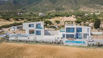 Uma casa moderna de dois andares com piscina, cercada por uma paisagem árida e montanhas.