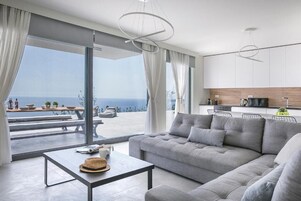 Uma sala de estar moderna com um sofá cinza, uma mesa de jantar e vista para o oceano.