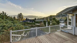 Um deck de madeira com guarda-corpo branco, com vista para uma área residencial com casas e árvores.