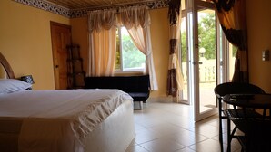 Quarto de hotel com cama, um banco, uma cadeira e porta que dá para uma varanda.