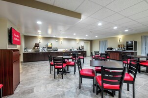 Quarto de hotel com cozinha compacta, área de refeições com cadeiras vermelhas e televisão exibindo 'Wi-Fi Gratuito em Todos os Quartos'.