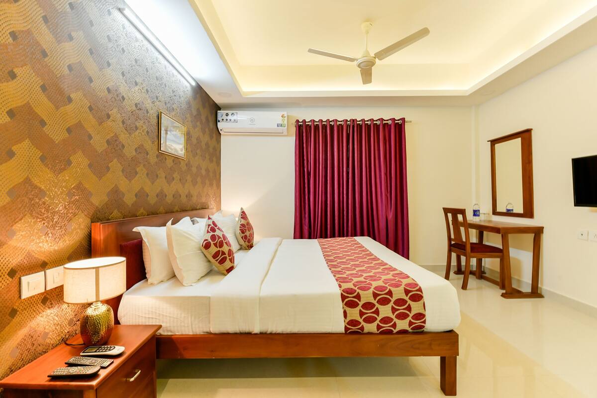 Quarto de hotel com cama, escrivaninha, cadeira, ventilador de teto e ar condicionado.