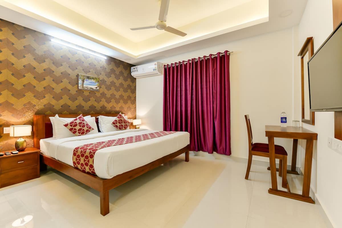 Quarto de hotel com cama, mesa de cabeceira, luminária, ar condicionado e escrivaninha com cadeira.