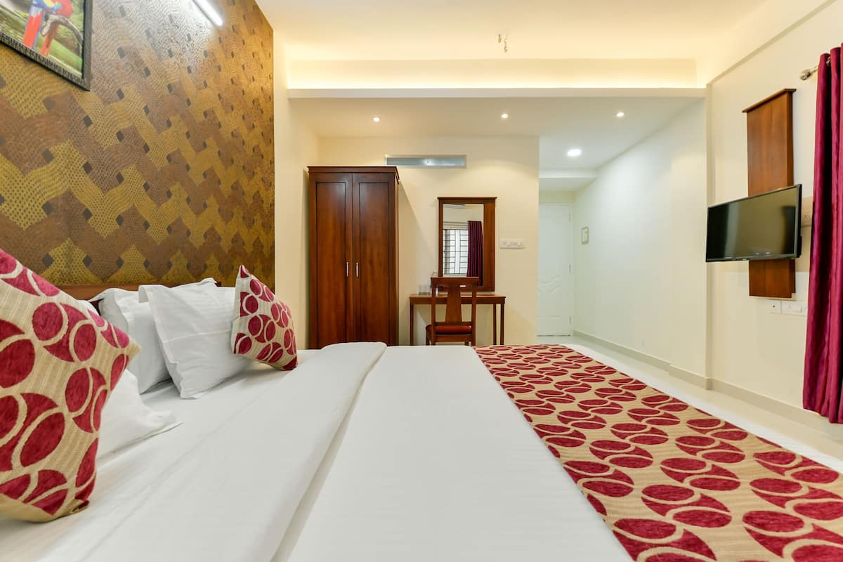 Quarto de hotel com uma cama, uma escrivaninha, uma televisão e um tapete estampado.