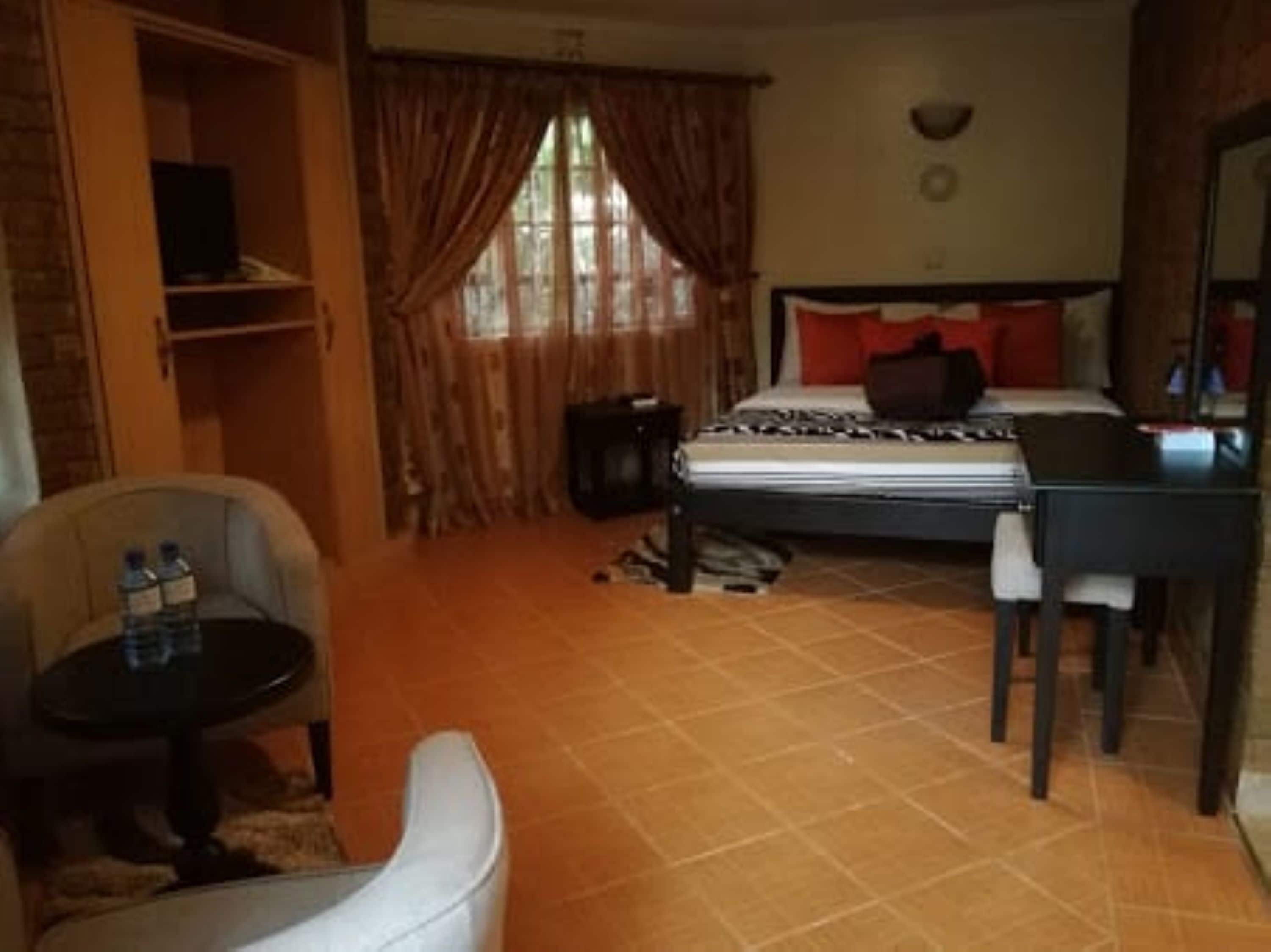 Quarto de hotel com cama, escrivaninha, cadeira, mesinha e guarda-roupa.