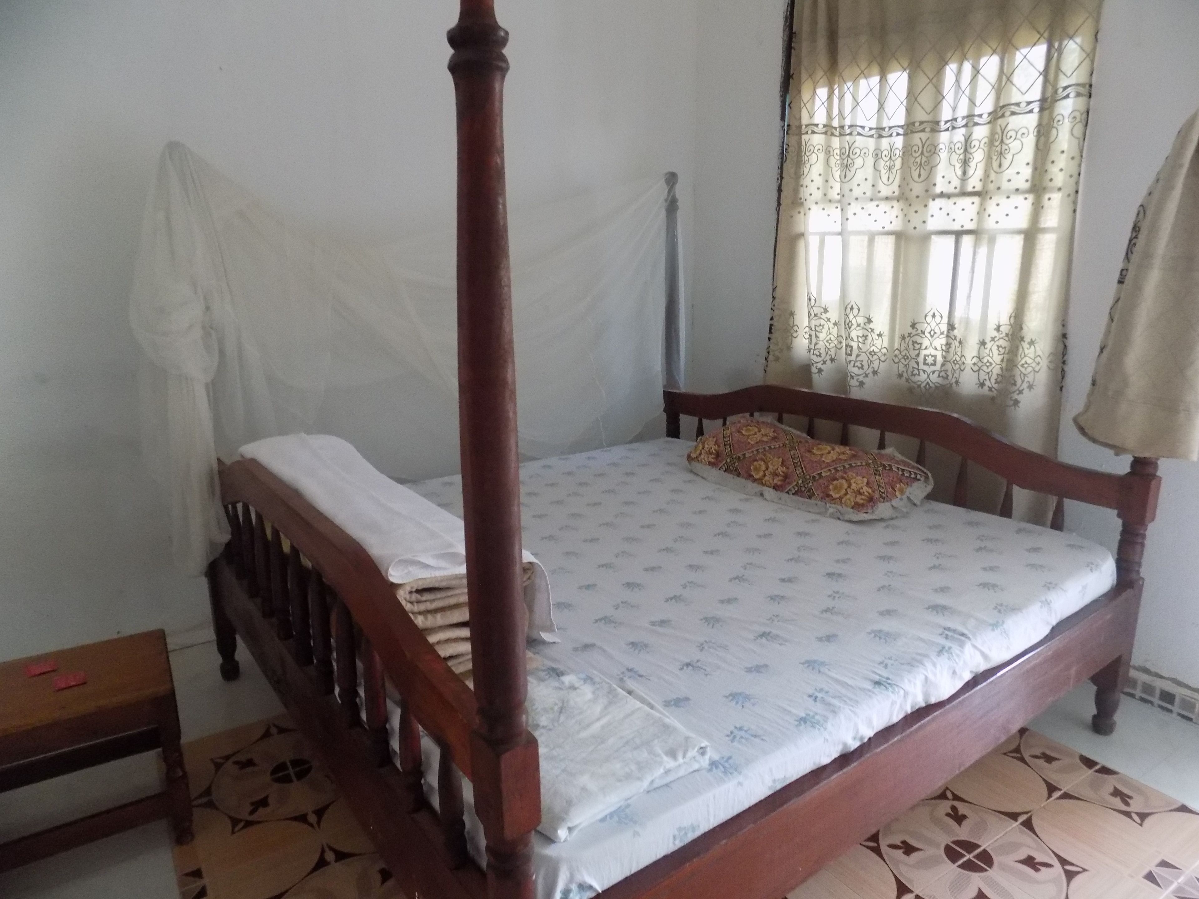 Uma cama de dossel com estrutura de madeira e colcha branca estampada com flores.