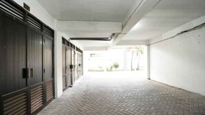 Um corredor com piso de tijolos, paredes brancas e uma porta à esquerda.