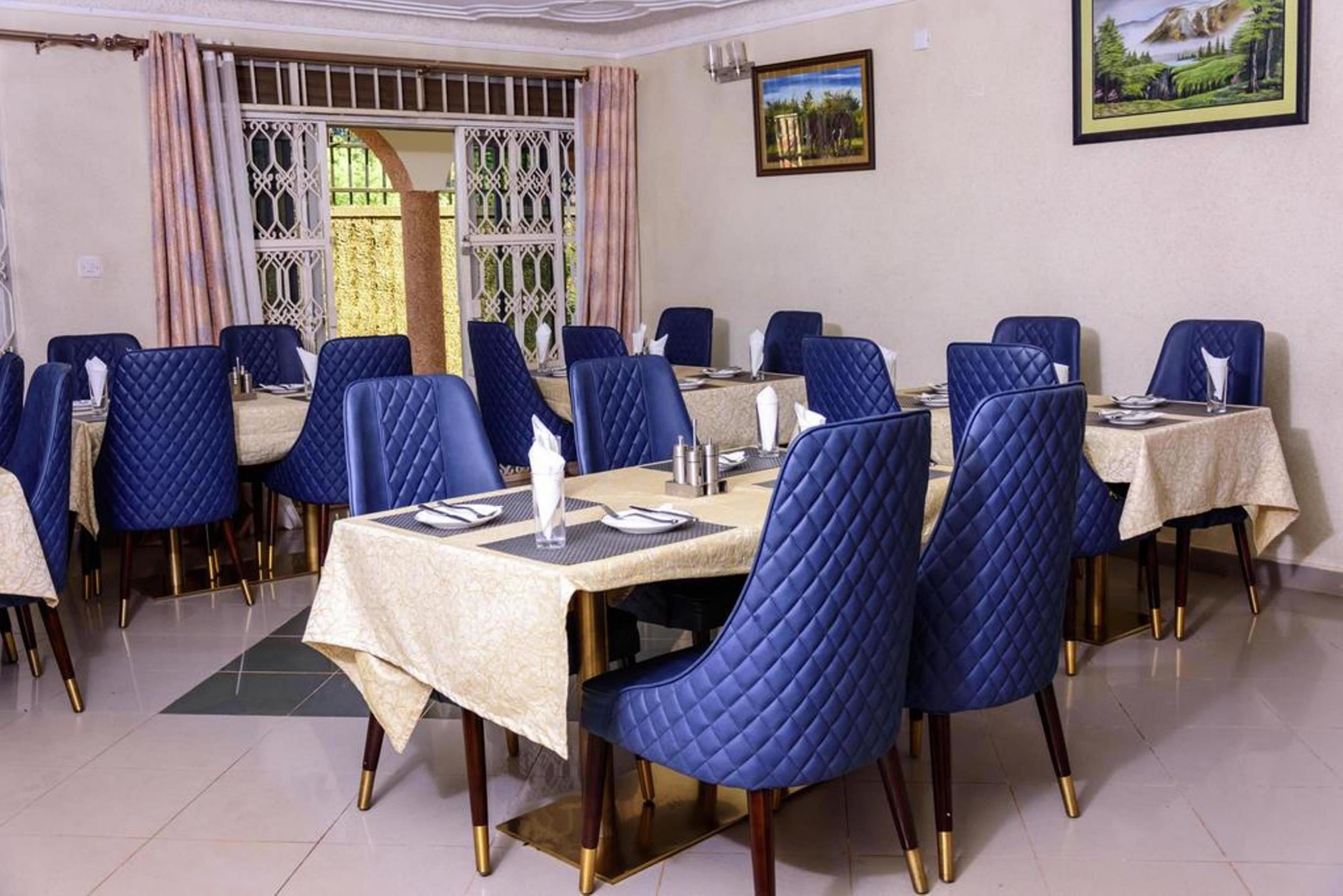 Uma sala de jantar com mesas postas para seis pessoas, cadeiras estofadas em azul e vista para o verde lá fora.