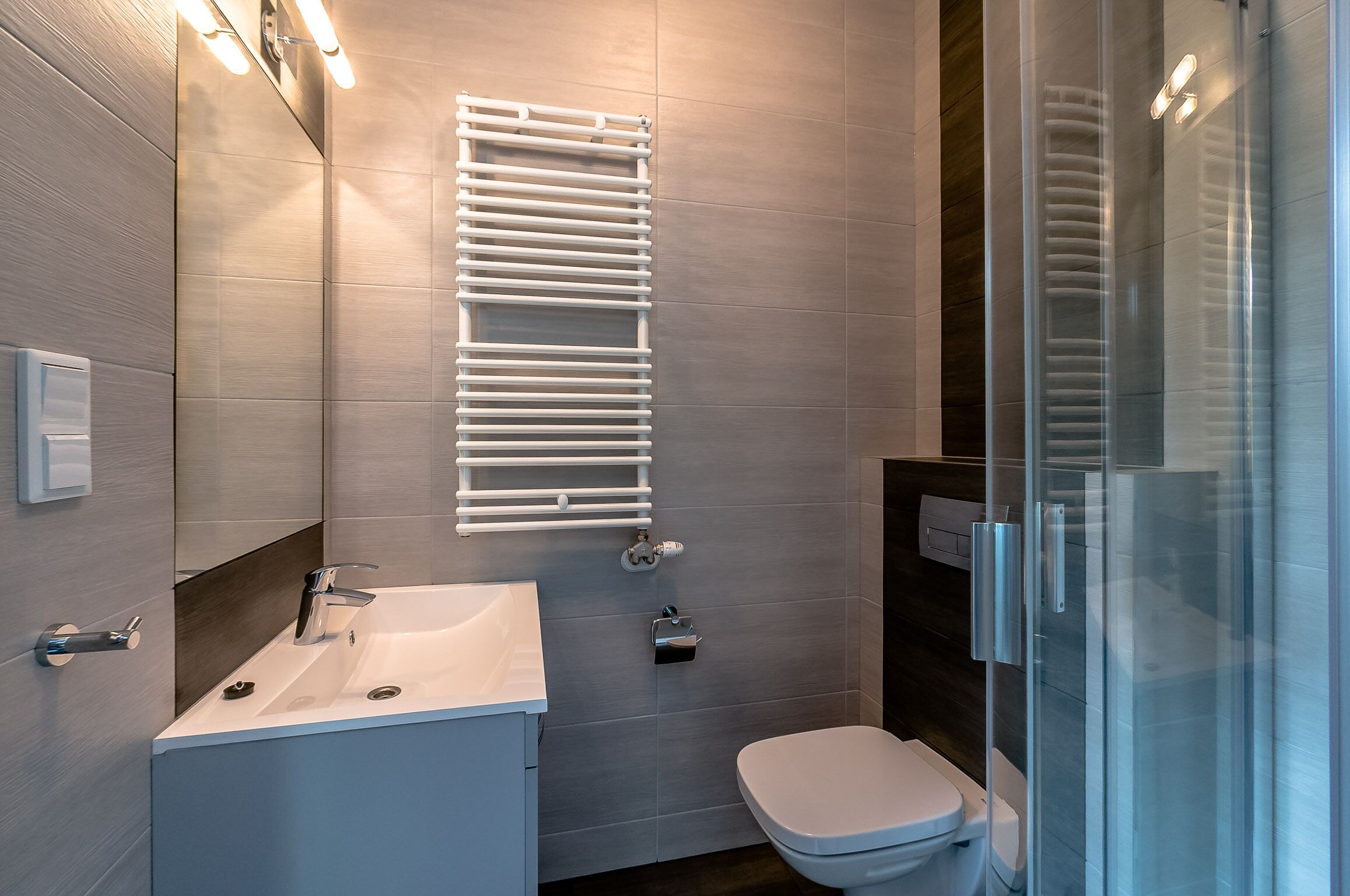 Uma casa de banho moderna com uma sanita branca, loiça sanitária e cabine de duche em vidro.