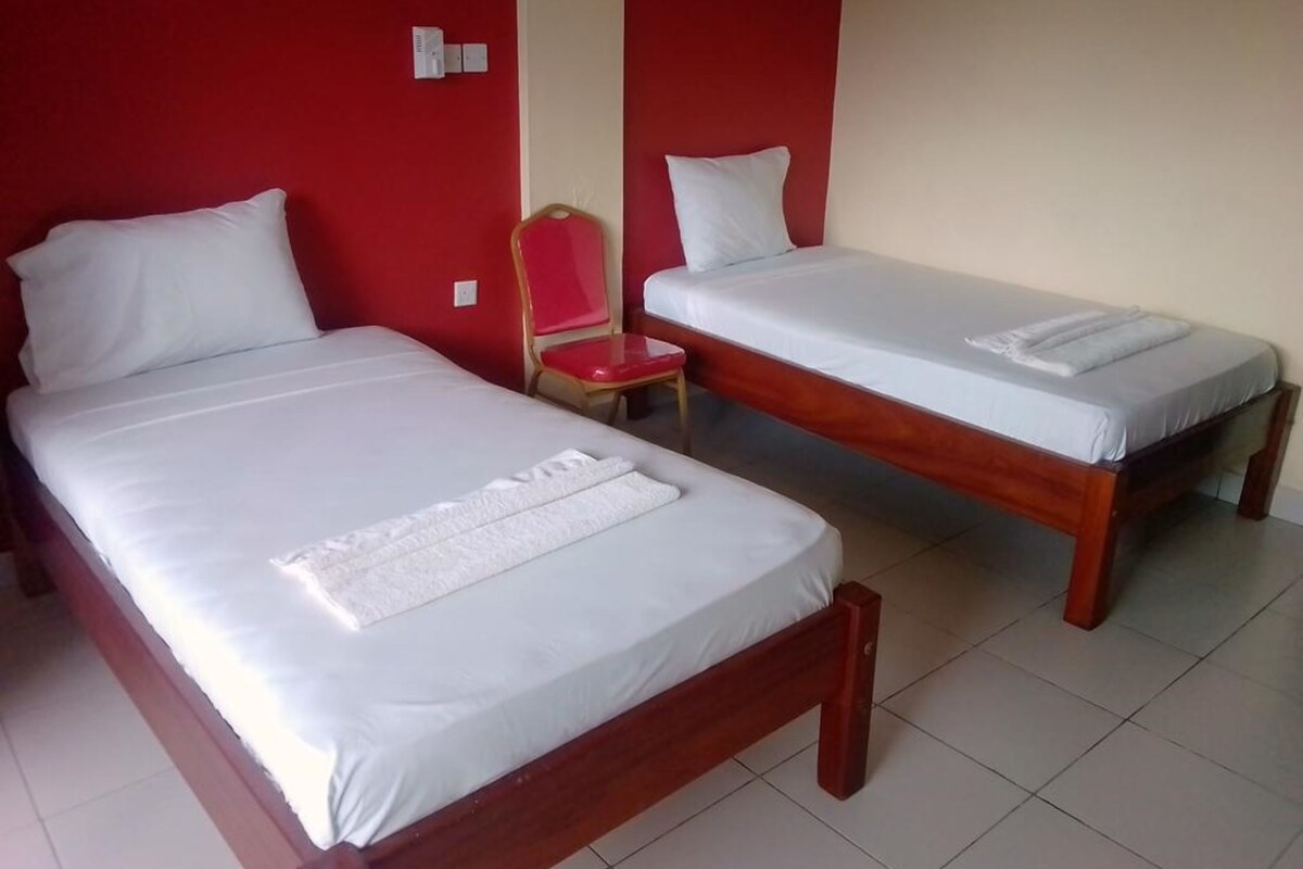 Quarto de hotel com duas camas, parede vermelha e chão em mosaico.
