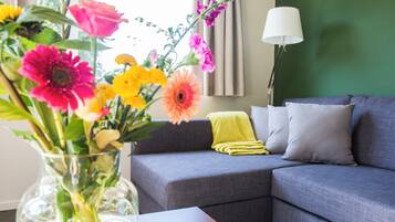 Uma sala de estar com um sofá cinzento, um cobertor amarelo e um vaso de flores.
